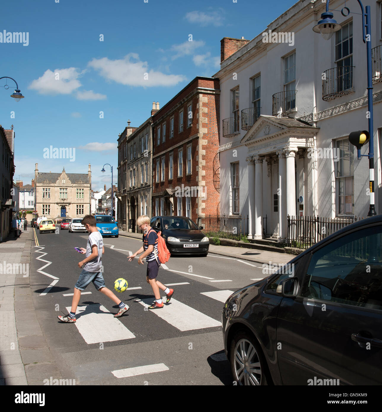 Young boys crossing the road on a panda crossing playing ball and using ...
