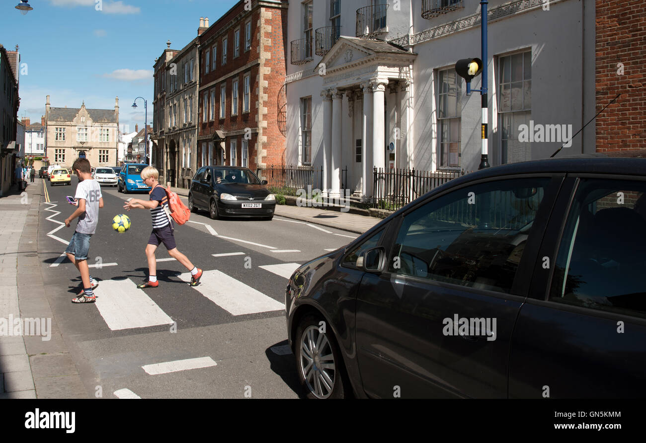 Young boys crossing the road on a panda crossing playing ball and using ...