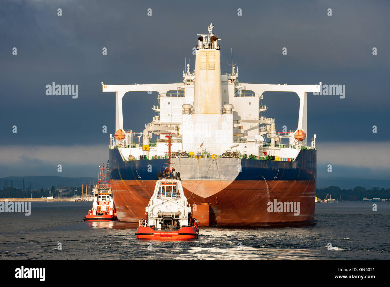 Tugboats towing a large tanker ship in port Stock Photo - Alamy