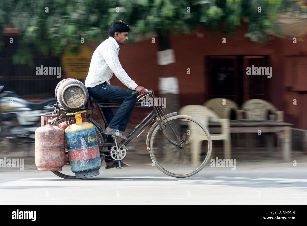 A cyclist riding his bike carrying full gas cylinders on a busy main ...