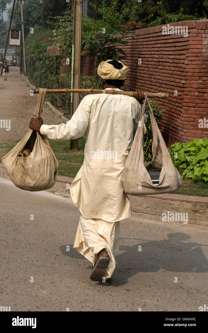 A snake charmer carrying his snakes in cloth sacking supported with a ...