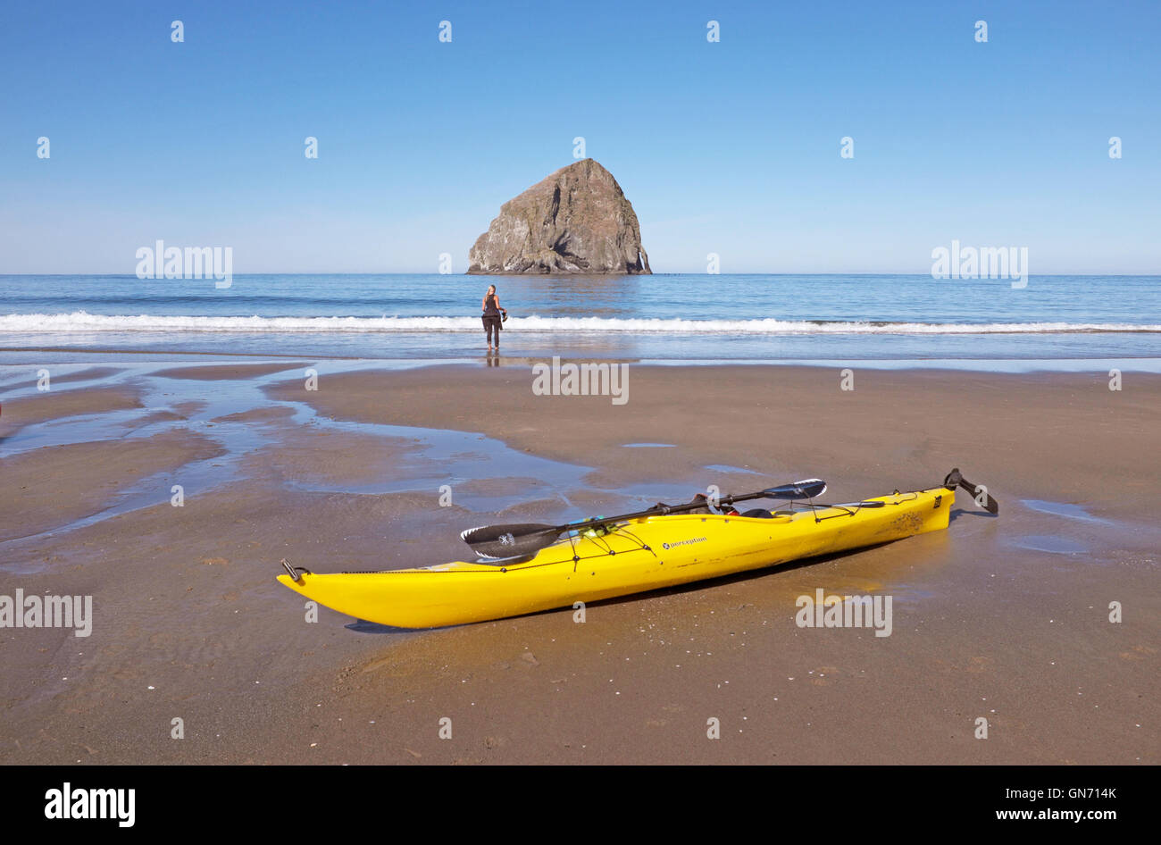 A sea kayak and kayaker on the beach in front of Haystack Rock, Pacific ...
