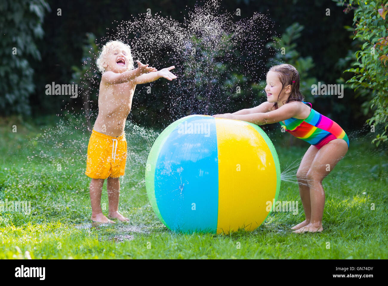 Child playing with toy ball garden sprinkler. Preschooler kid run and ...