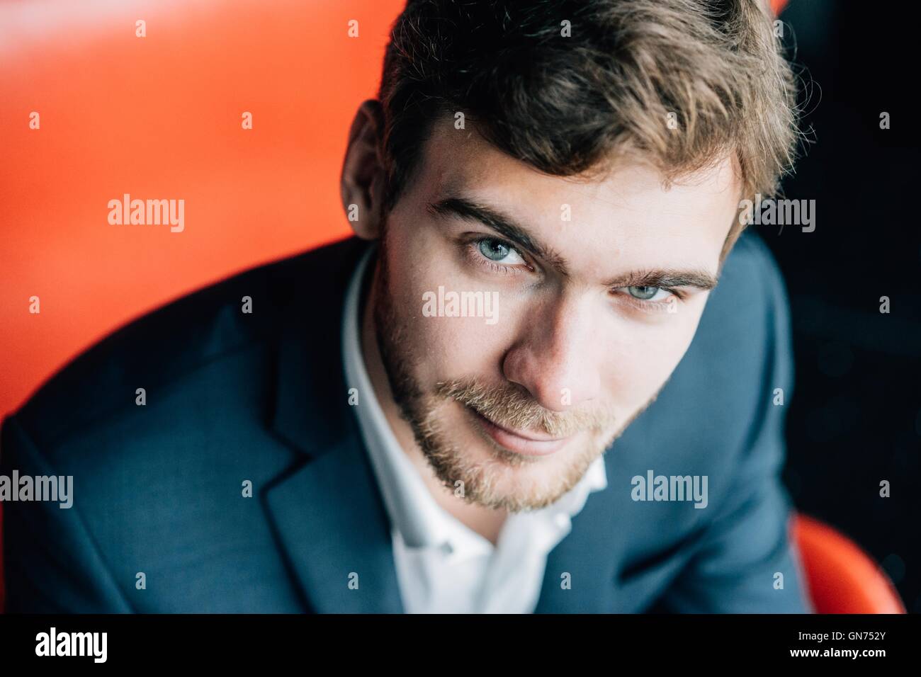 Portrait of young business man seated on a red chair Stock Photo - Alamy