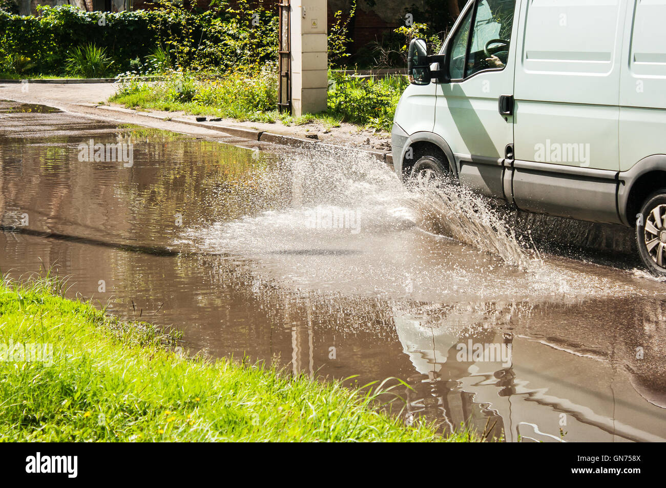 white commercial vehicle riding on big puddle on the road in residental ...