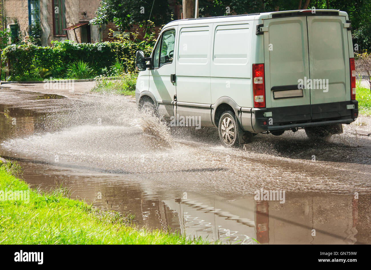 white commercial vehicle riding on big puddle on the road in residental ...