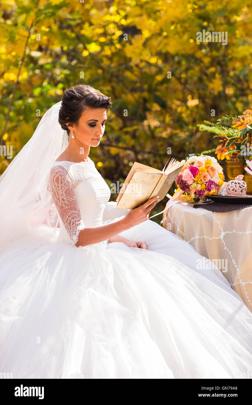 Pretty bride reading a book and enjoy in autumn park Stock Photo - Alamy