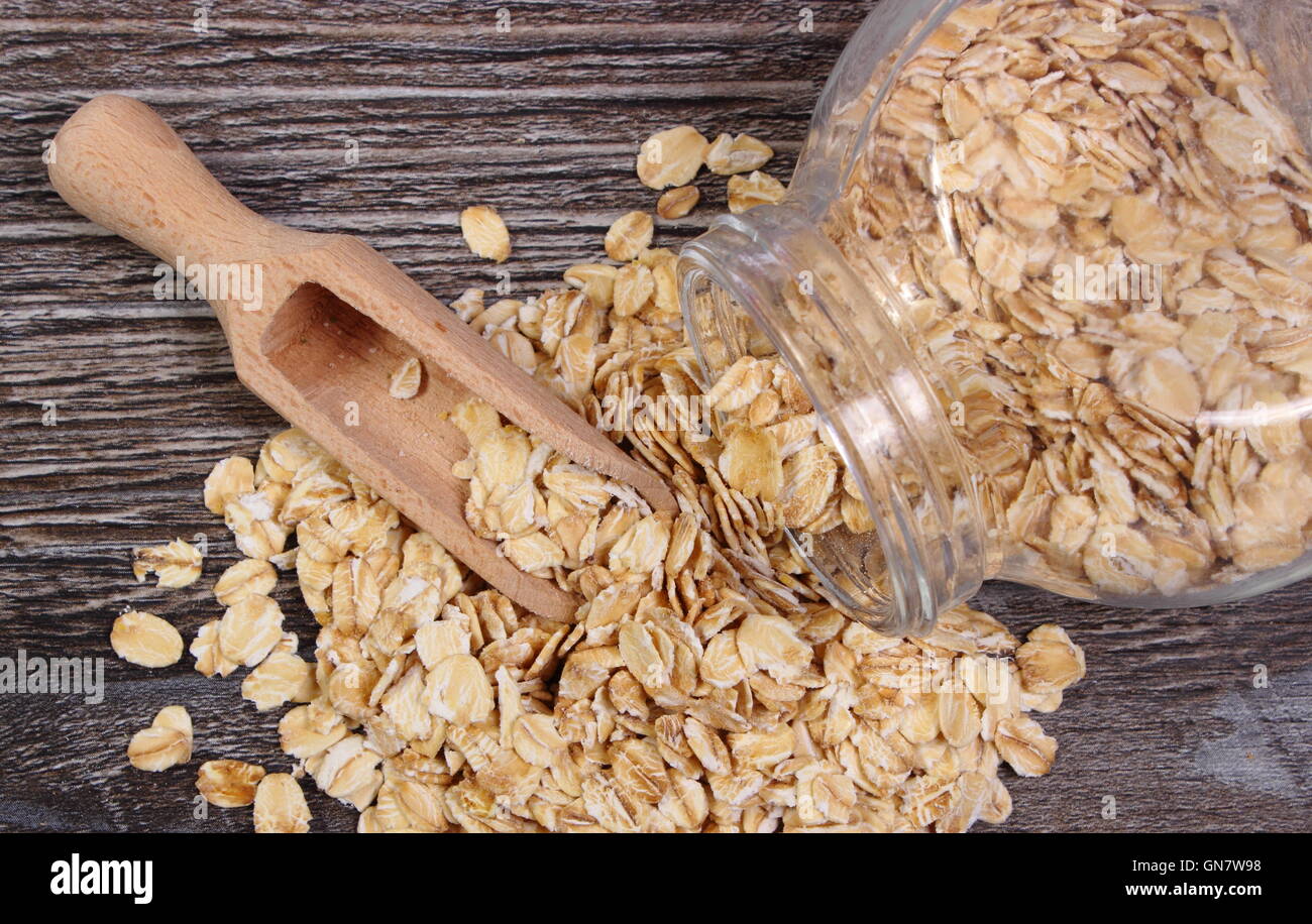 Heap of organic oatmeal, oat flakes spilling out of glass jar on wooden ...