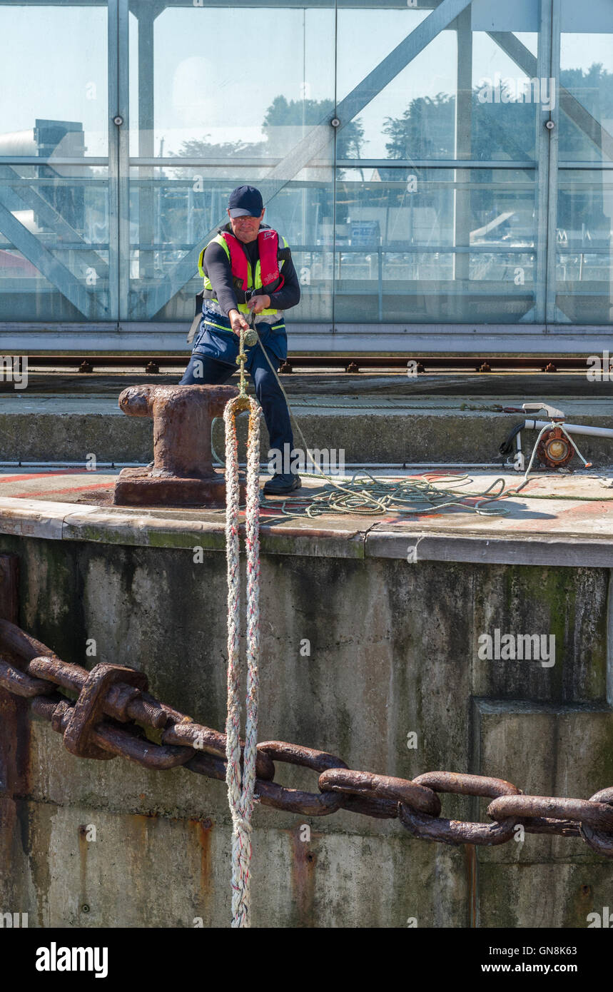 French dock worker pulls on the mooring rope of a docking car ferry ...