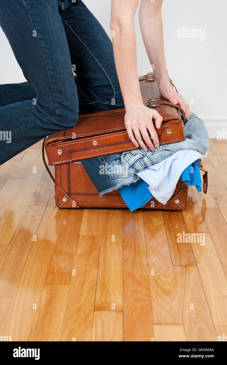 Woman trying to close suitcase with too much clothing Stock Photo - Alamy