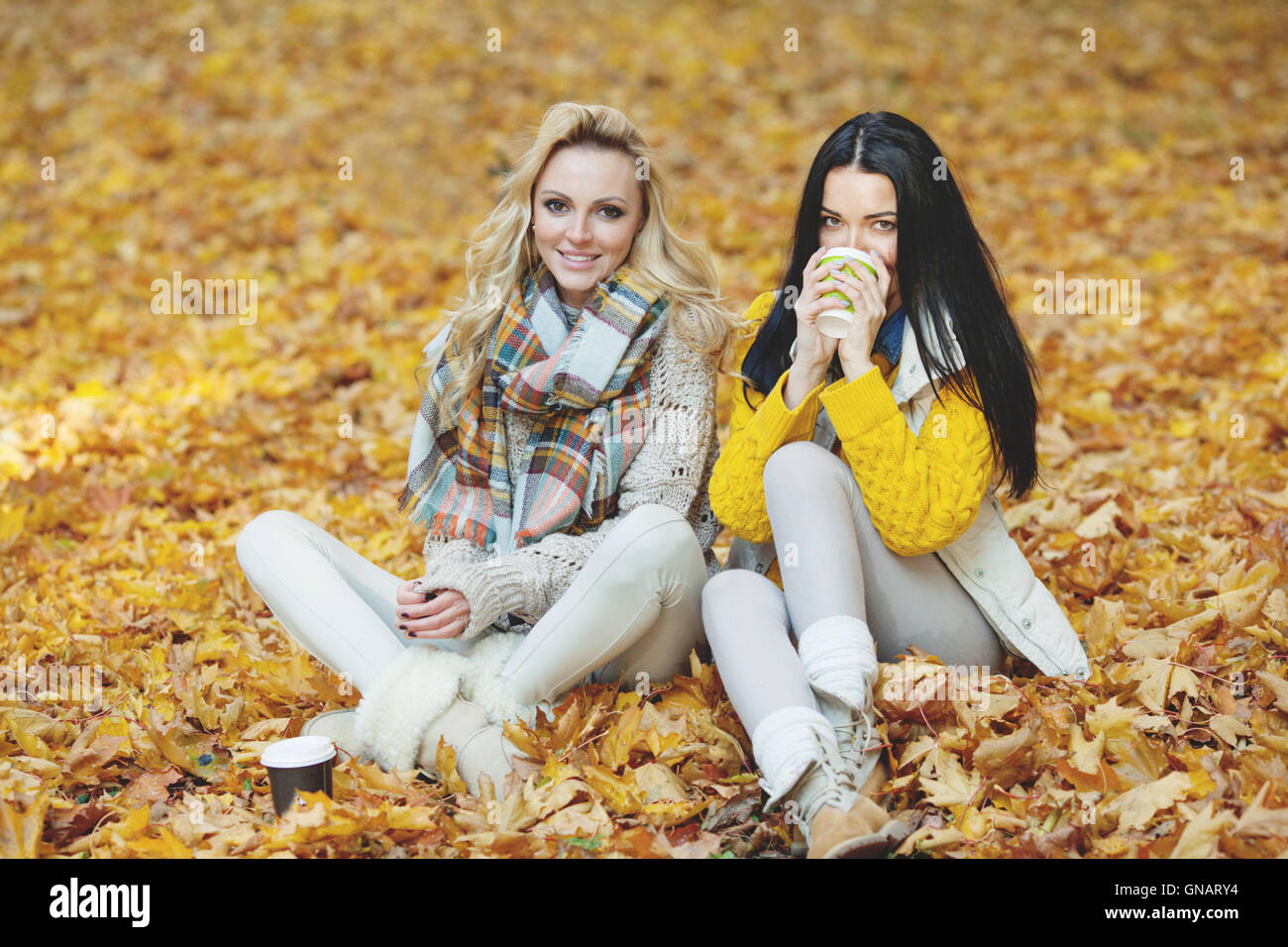 Two cheerful female friends drinking coffee in autumn park Stock Photo ...