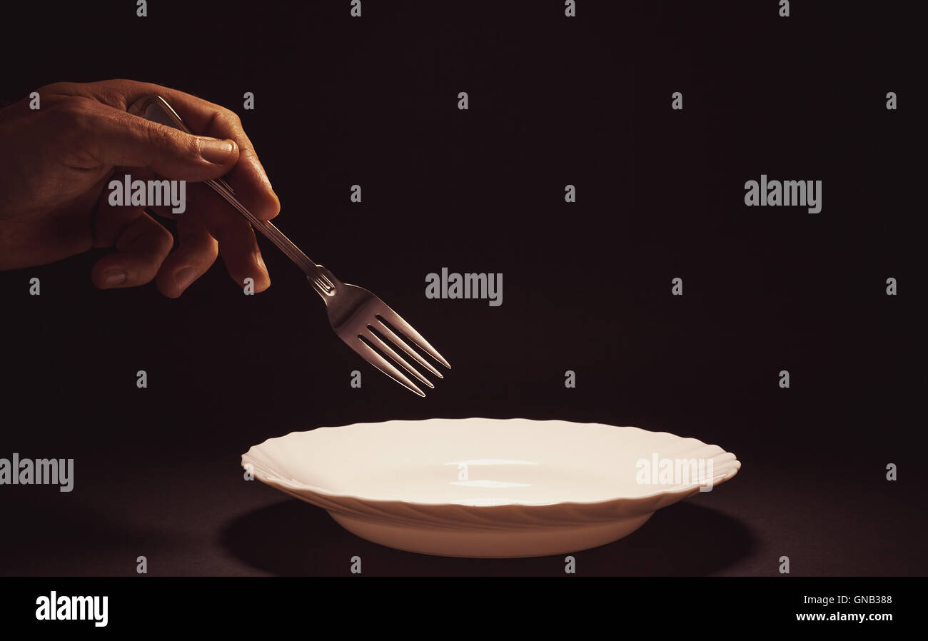 Conceptual composition, man's hand holding a metal fork over an empty ...