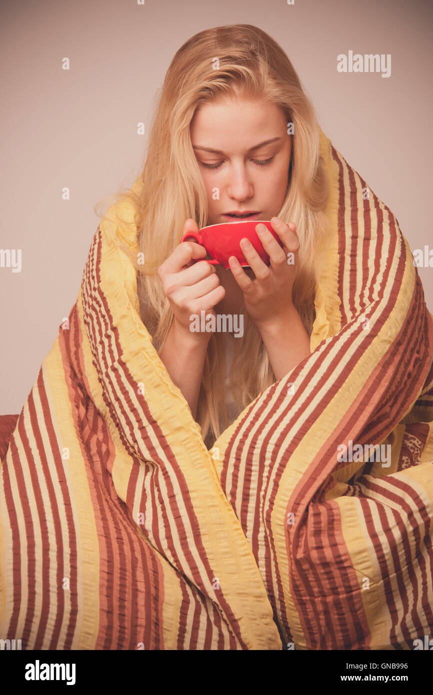 Sick woman sitting on bad wrapped in a blanket feeling ill, has flu and ...