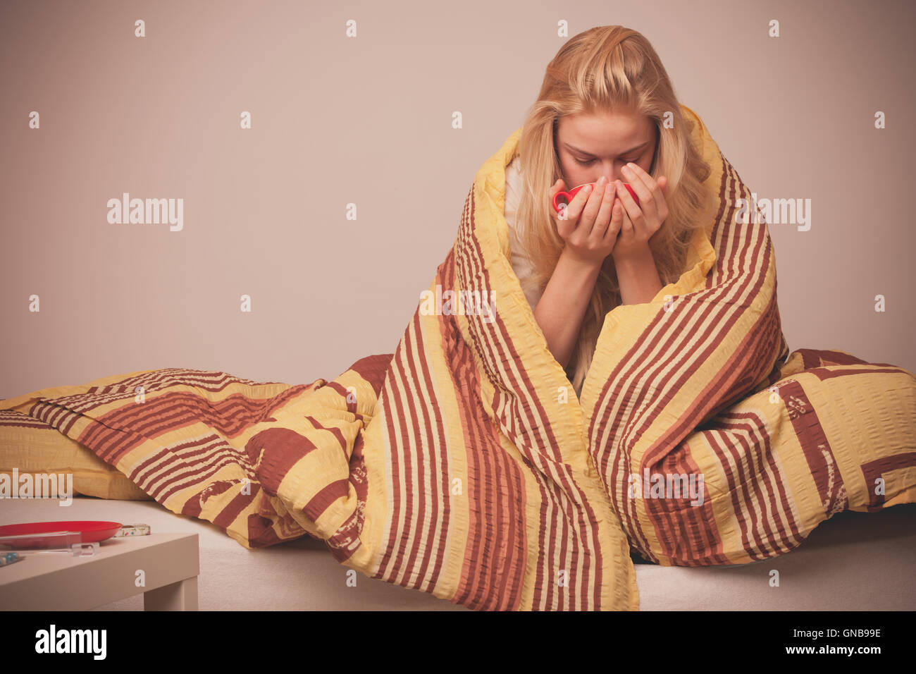 Sick woman sitting on bad wrapped in a blanket feeling ill, has flu and ...
