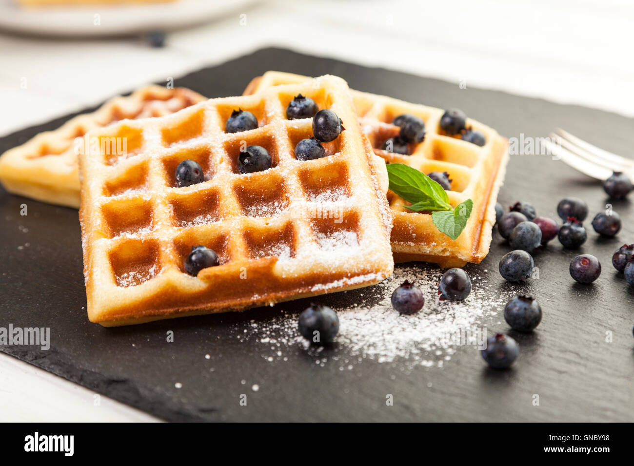 Belgian waffles with blueberries and powdered sugar on black slate ...