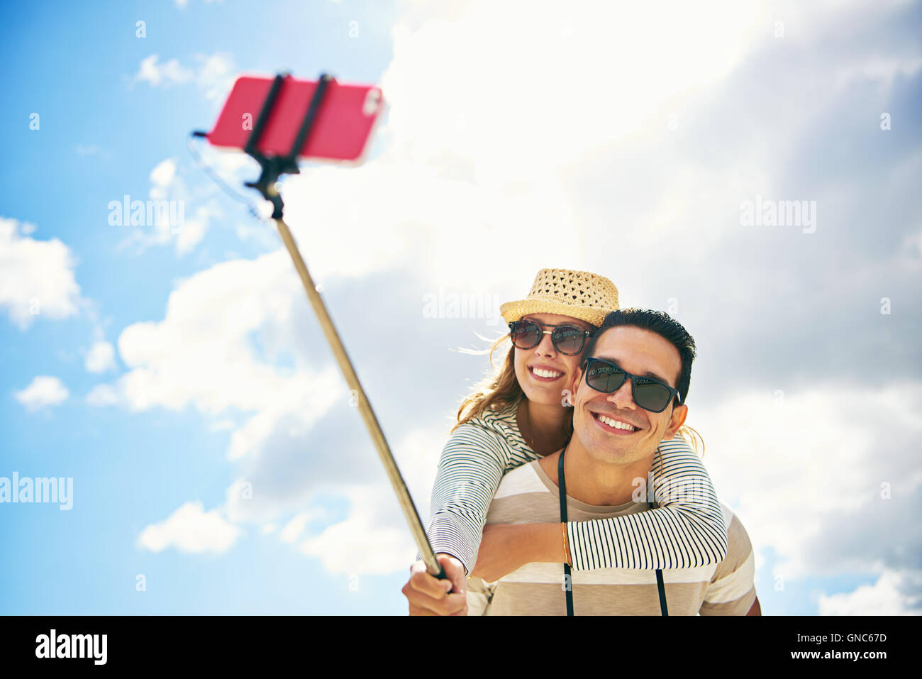 Young woman enjoying a piggy back ride clasping the shoulders of a handsome young man as they ...