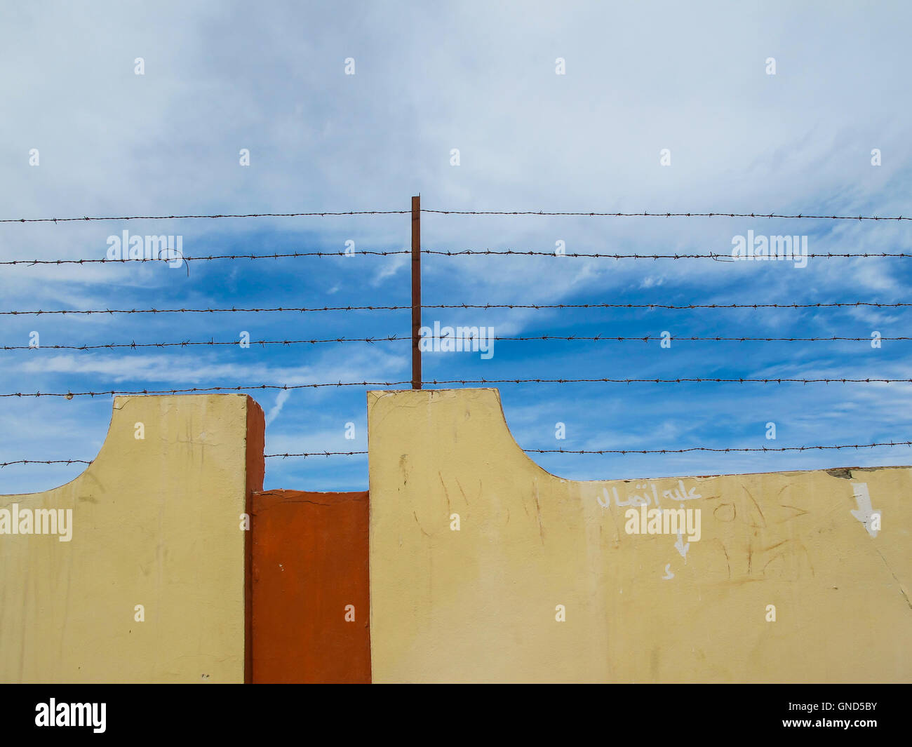 Yellow color of the fence with a barbed wire on the top. Blue sky with ...