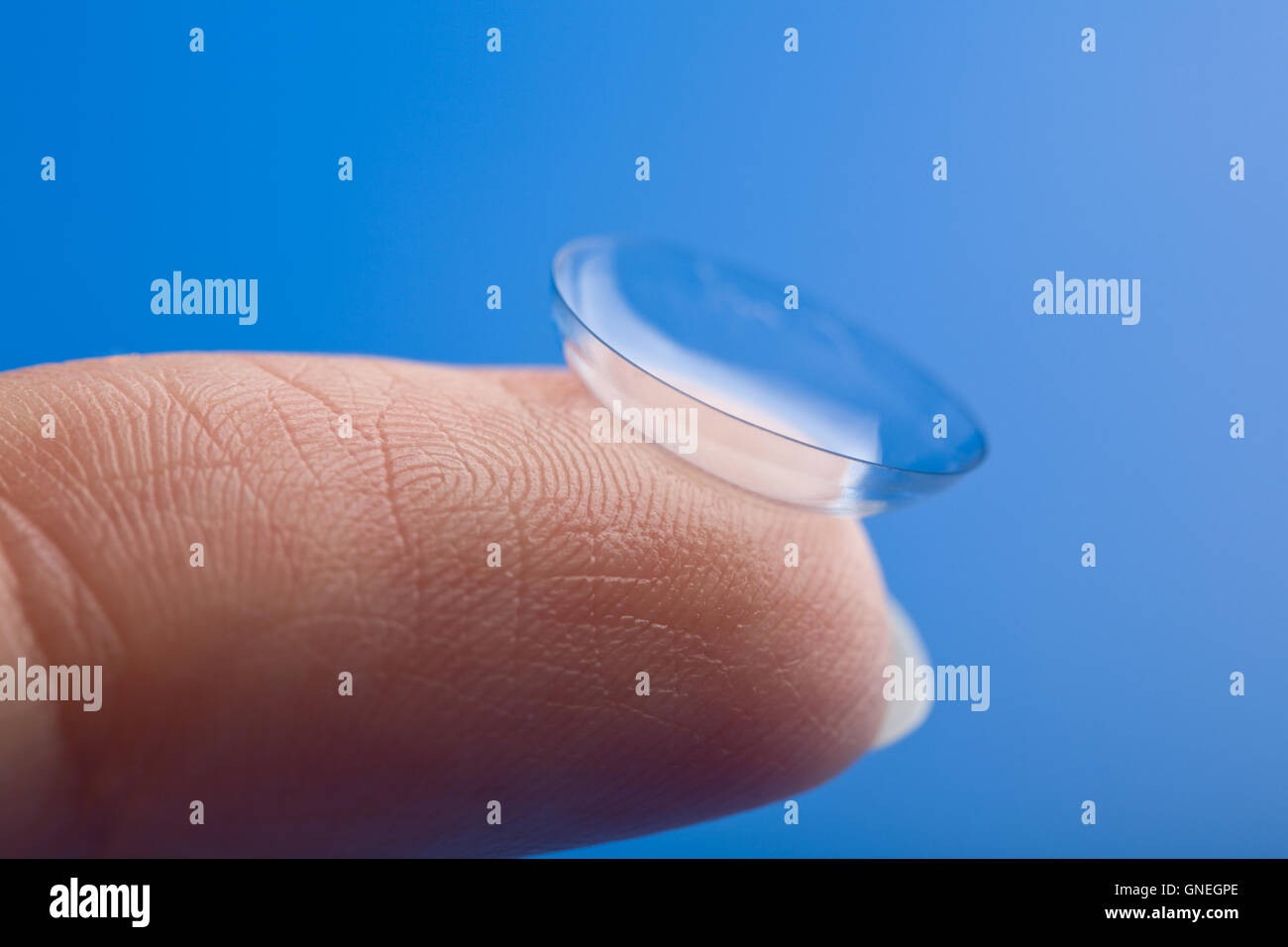 finger holding contact lens over blue background Stock Photo - Alamy