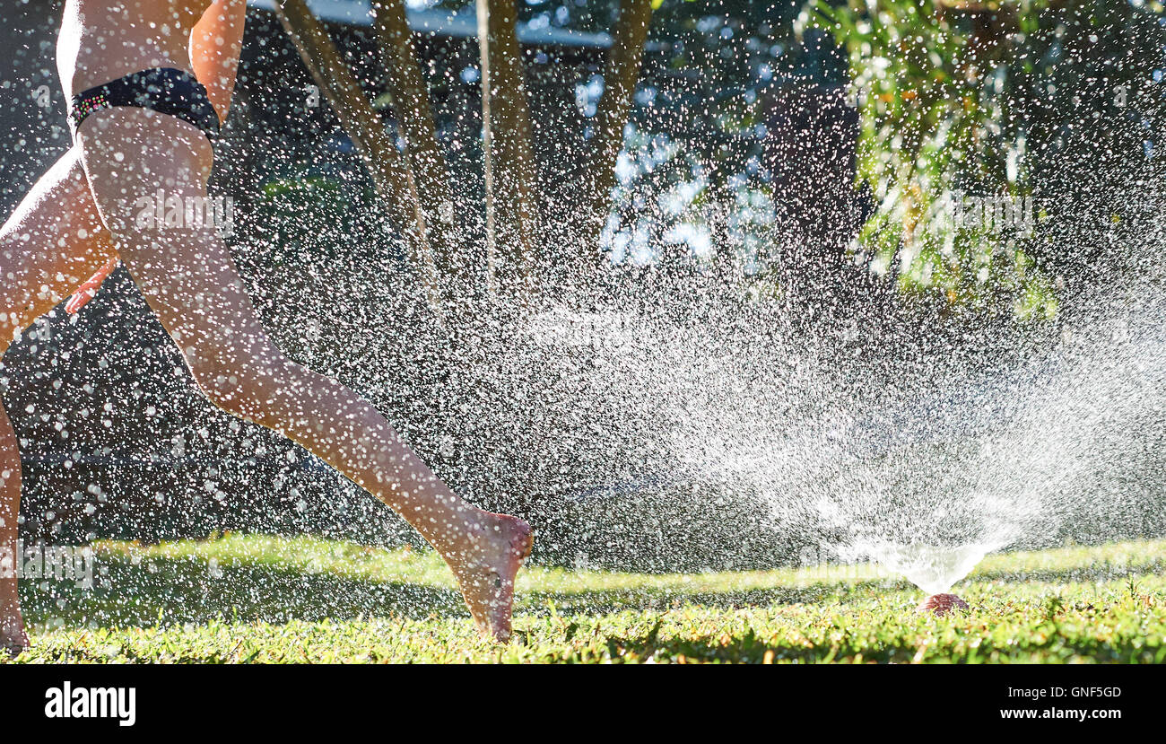 Young girl playing jumping in a garden water lawn sprinkler Stock Photo ...