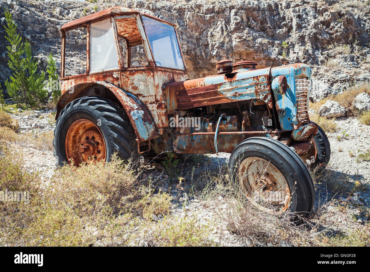 Old abandoned rusted tractor stands on dry summer grass, side view ...