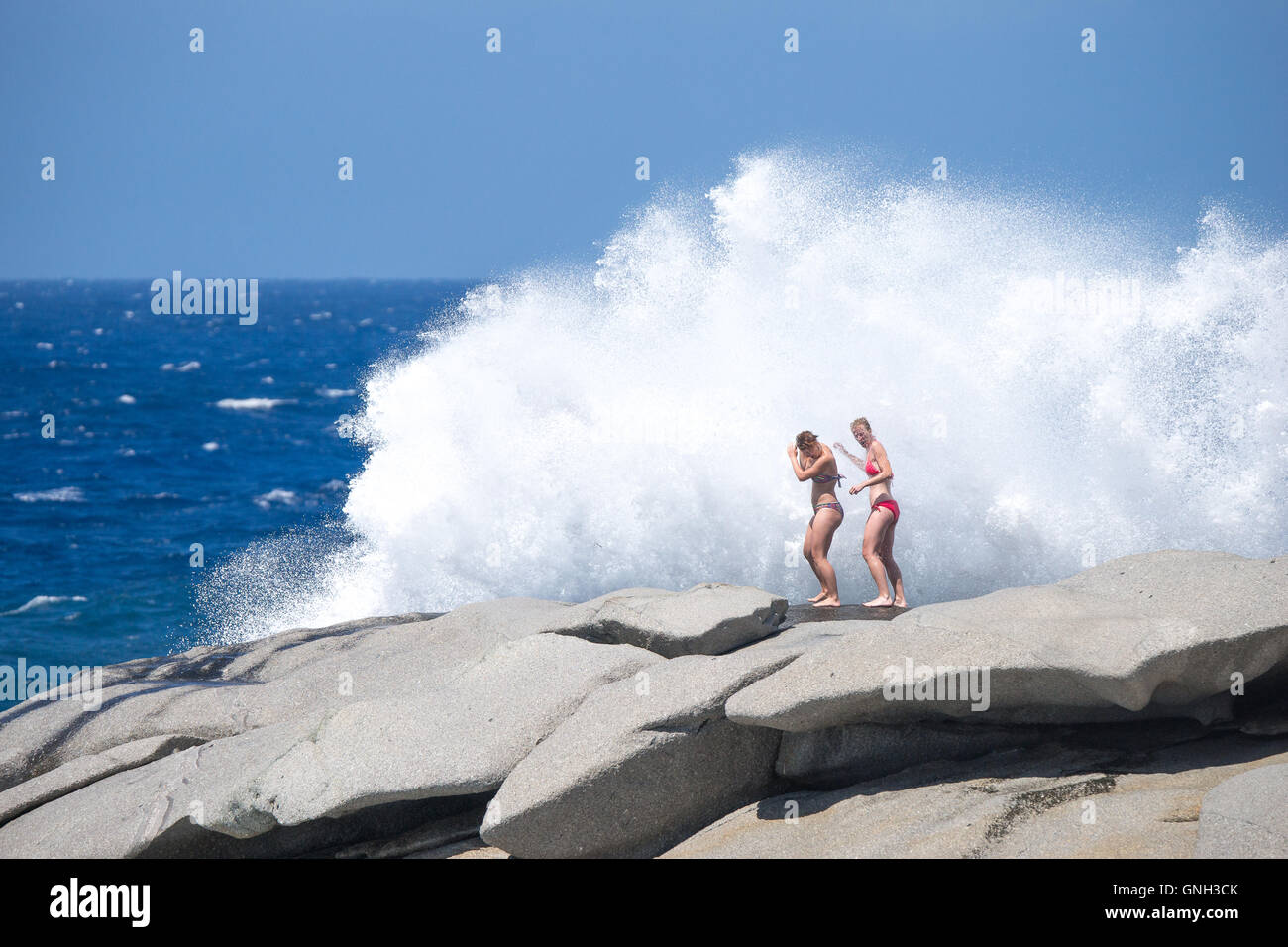 Two women standing on rocks hit by large wave, Corsica, France Stock ...