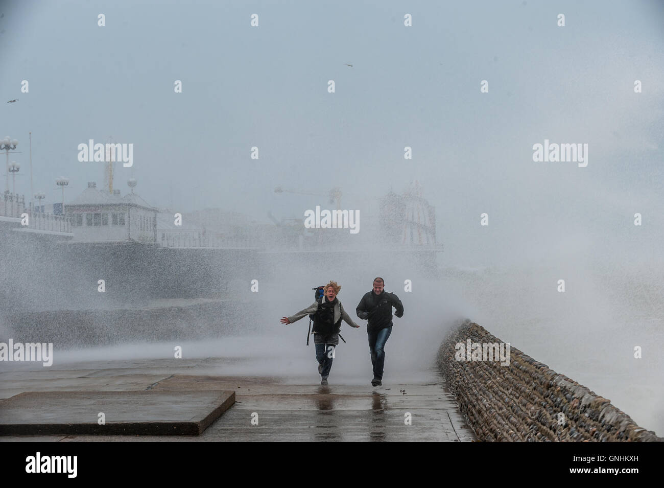 A couple run to escape the waves on the seafront at Brighton Stock ...