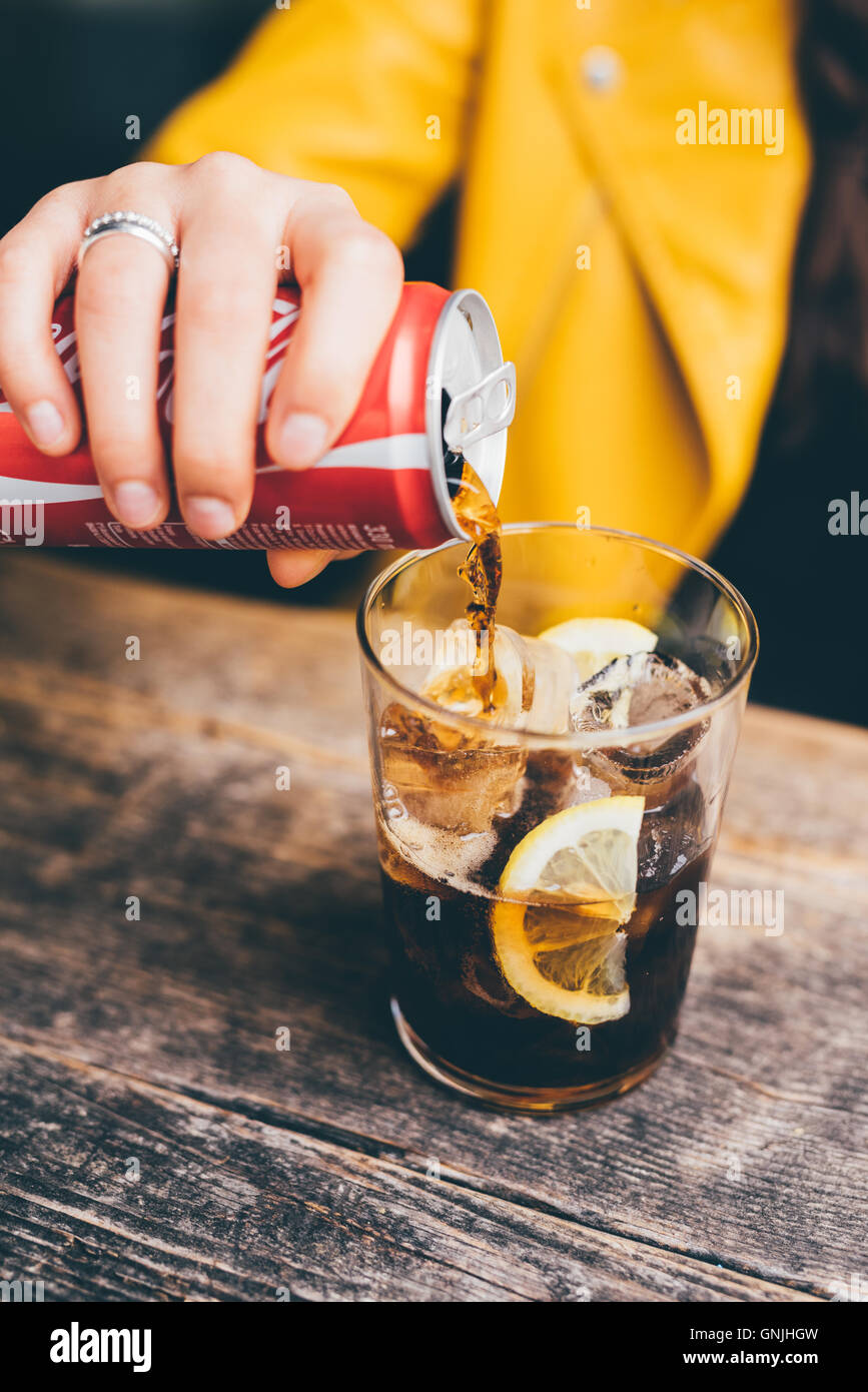 Close up on the hand of young woman porung soft drink into a glass with ...