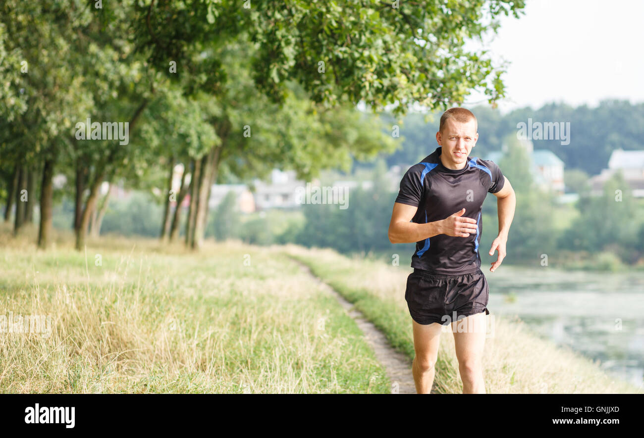 Young athletic man jogging in morning park. Running training outdoors panoramic image with copy ...