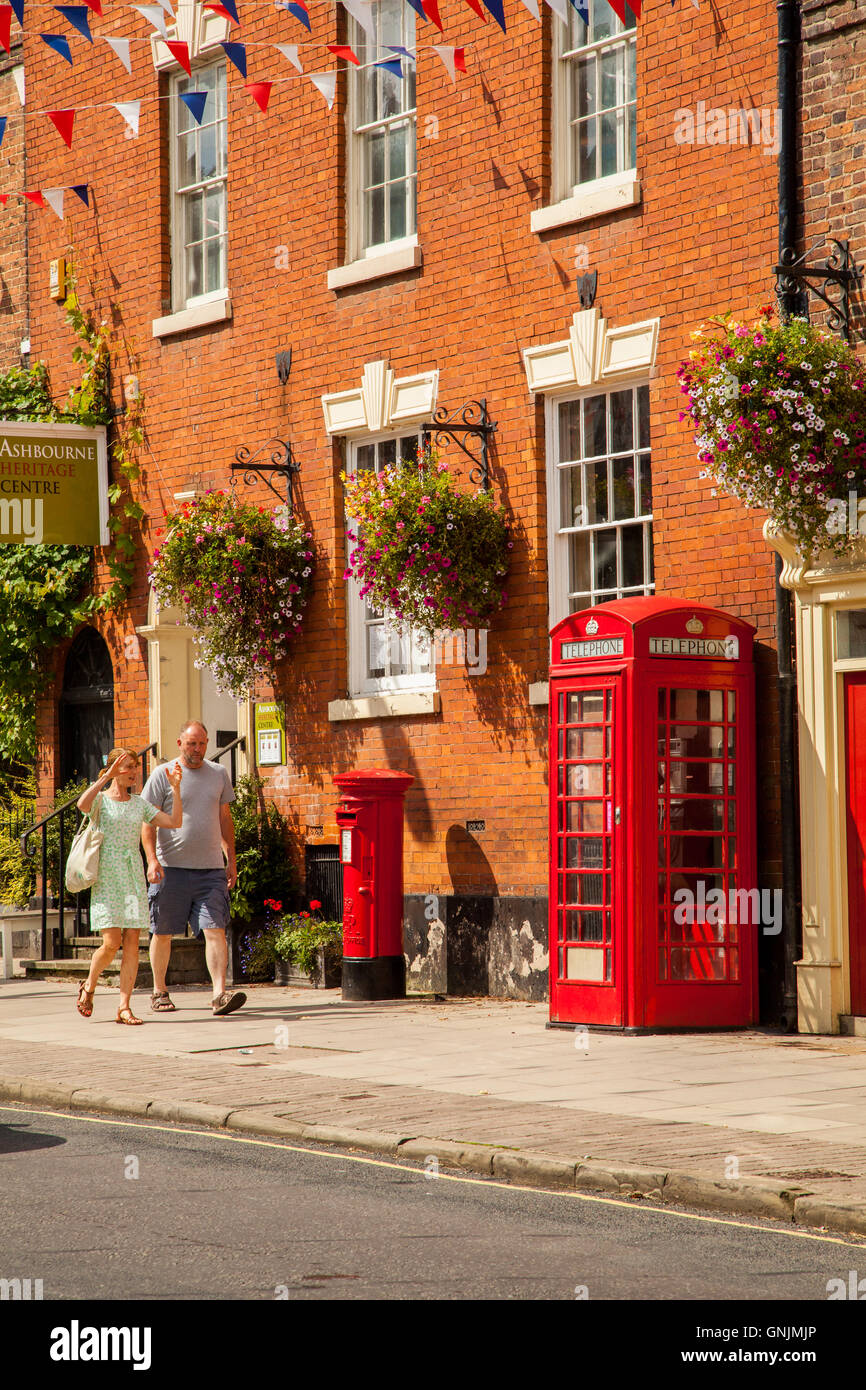 Man and women walking past red round post box and traditional red ...