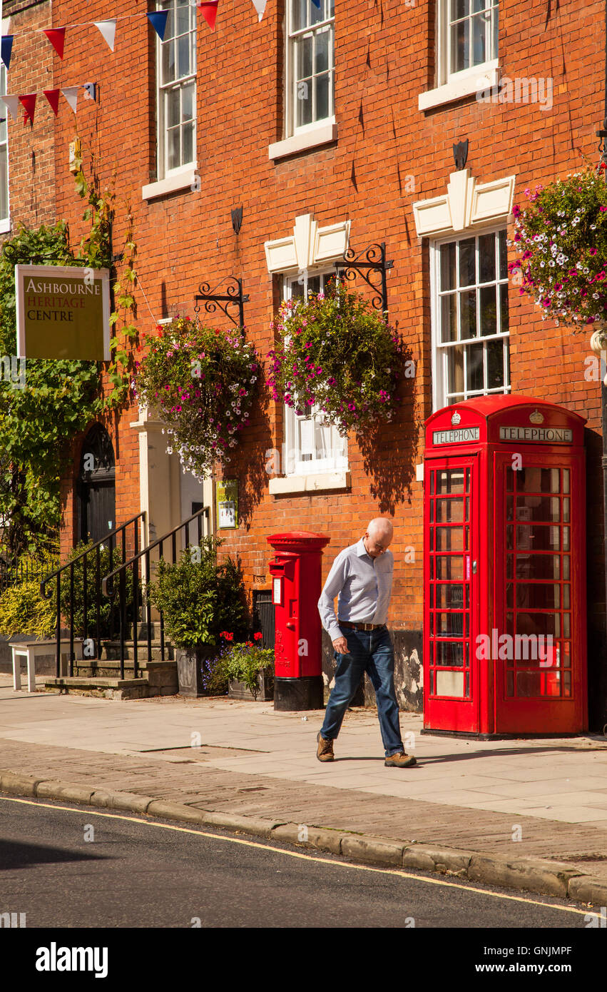 Man walking past Red round post box and traditional red telephone box ...