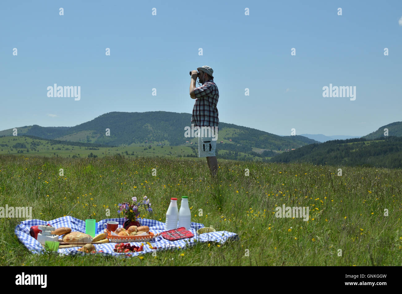 Man watching landscape with binoculars on picnic with hills in ...