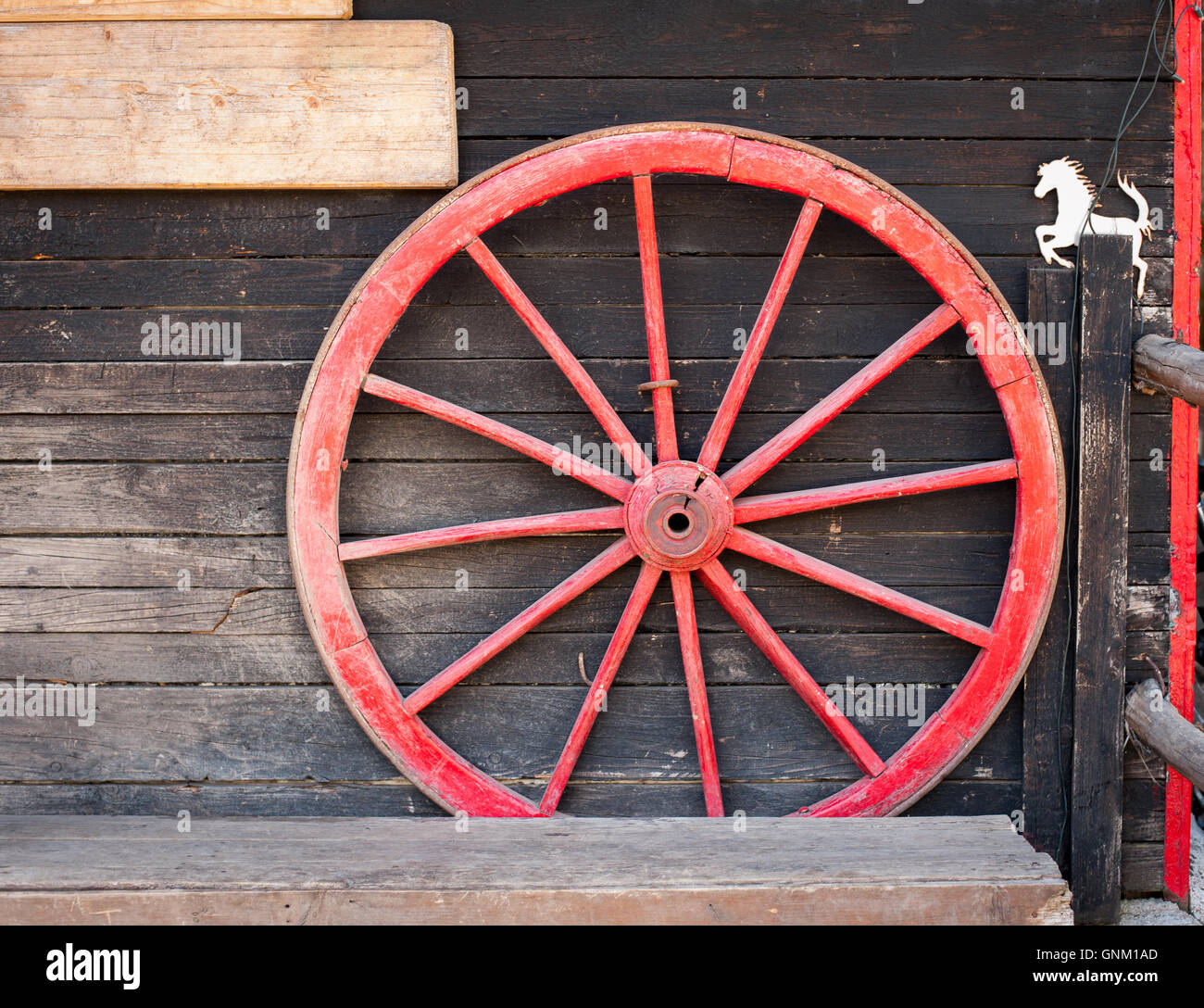 Big red cart wheel on wooden wall with little white horse, symbol ...