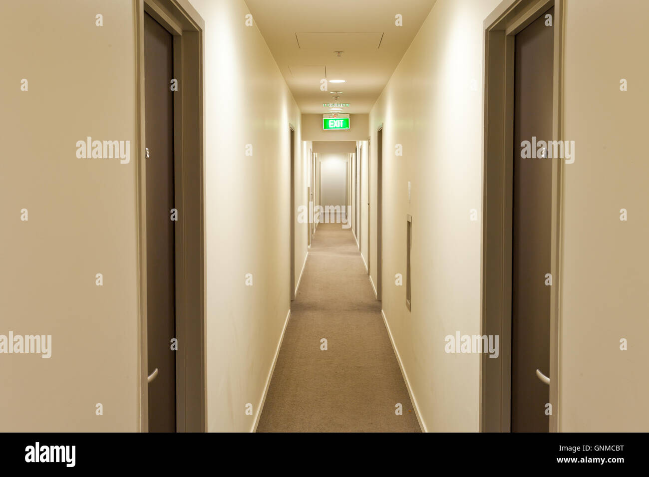Long corridor with hotel room doors and exit sign Stock Photo - Alamy