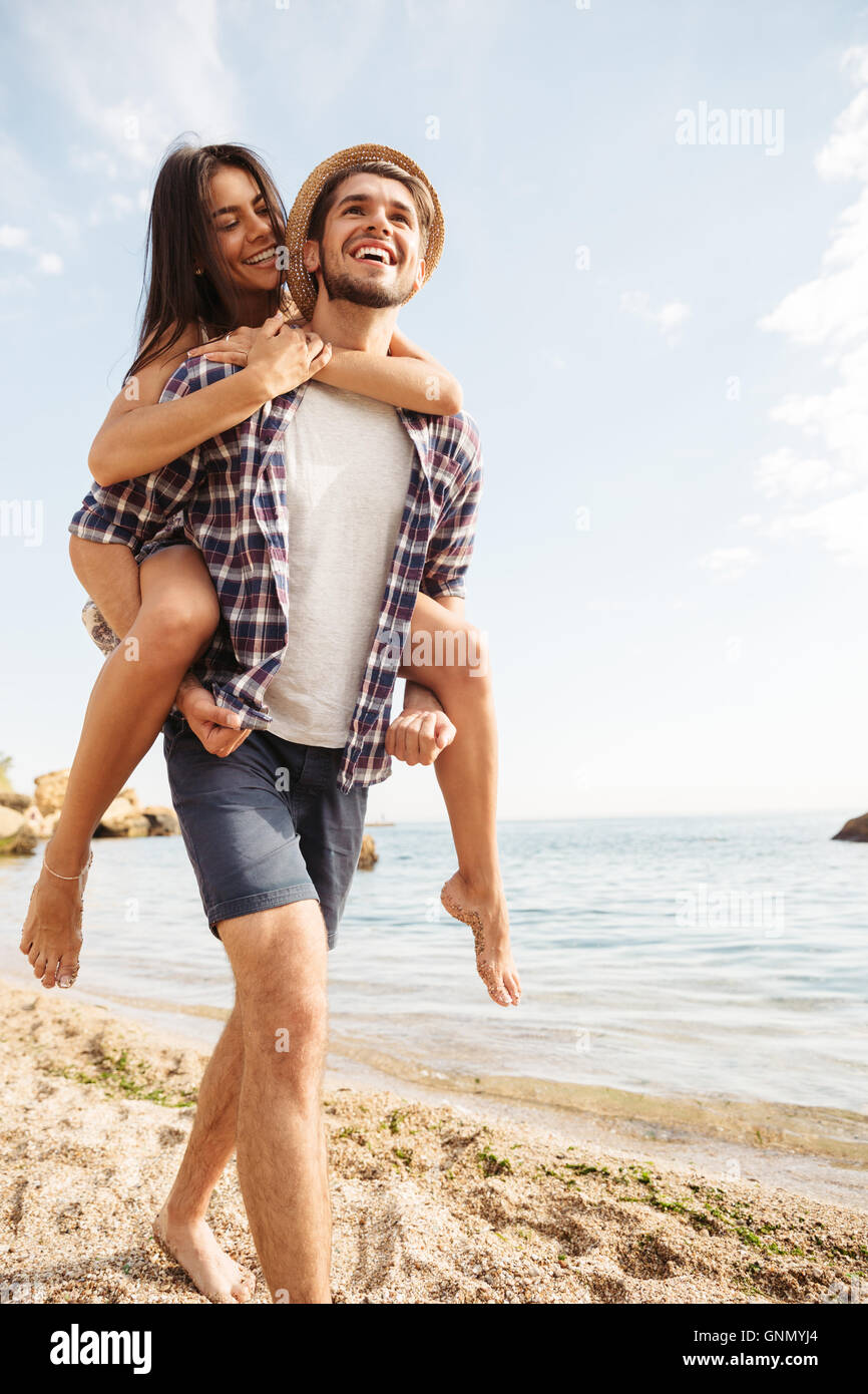 Handsome smiling young man giving piggy back ride to his girlfriend at the beach Stock Photo - Alamy