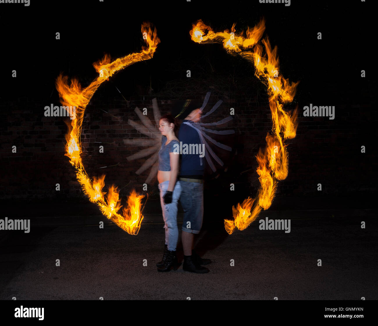 Two fire dancers spin poi in unison in darkness surrounded by ring of ...