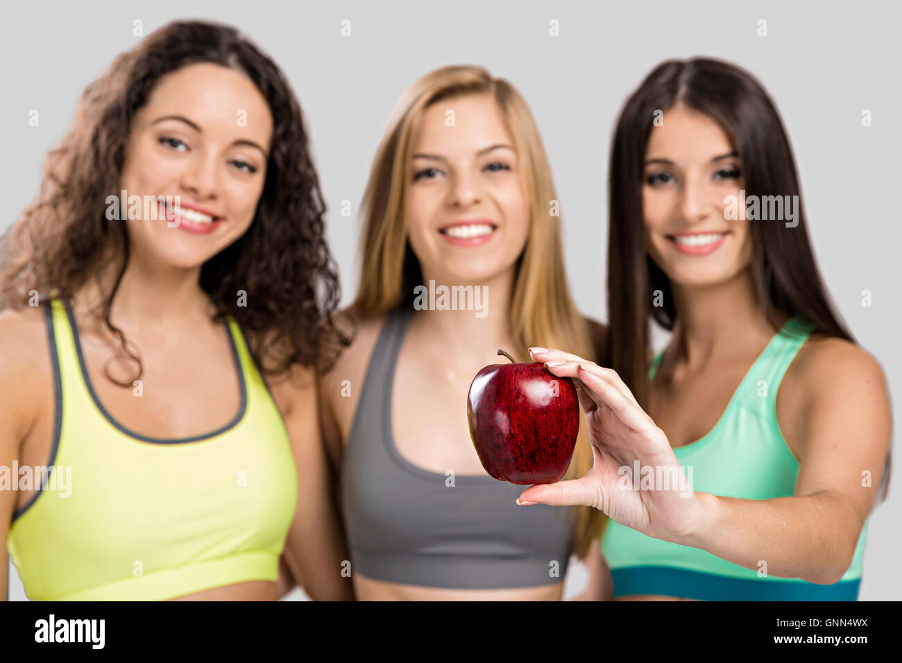 Portrait of three beautiful and athletic girls holding a red apple ...