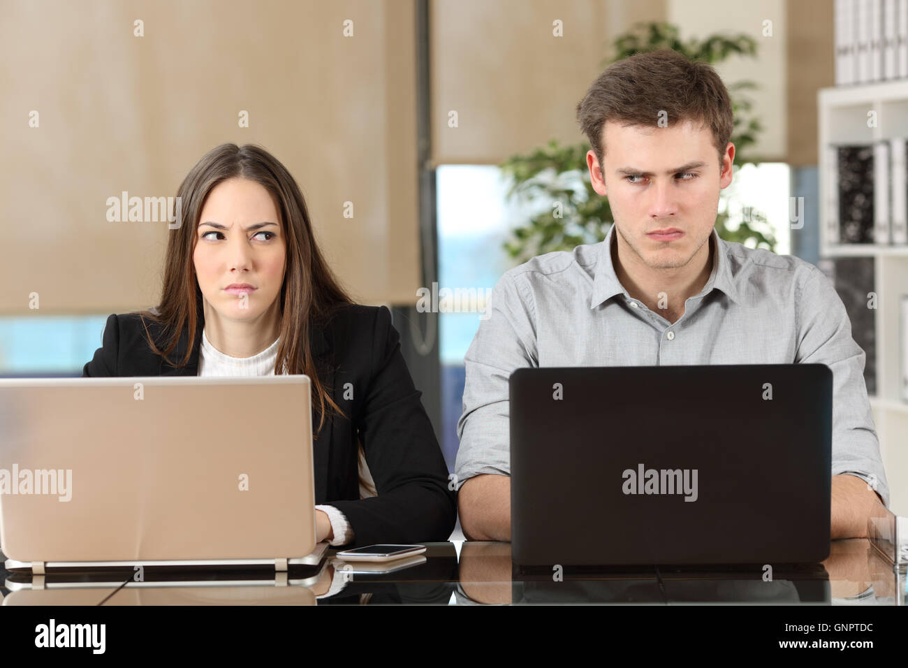 Front view of two angry businesspeople using computers disputing at ...