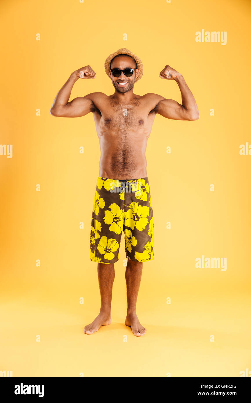Strong african young guy in swimwear showing muscles over orange ...