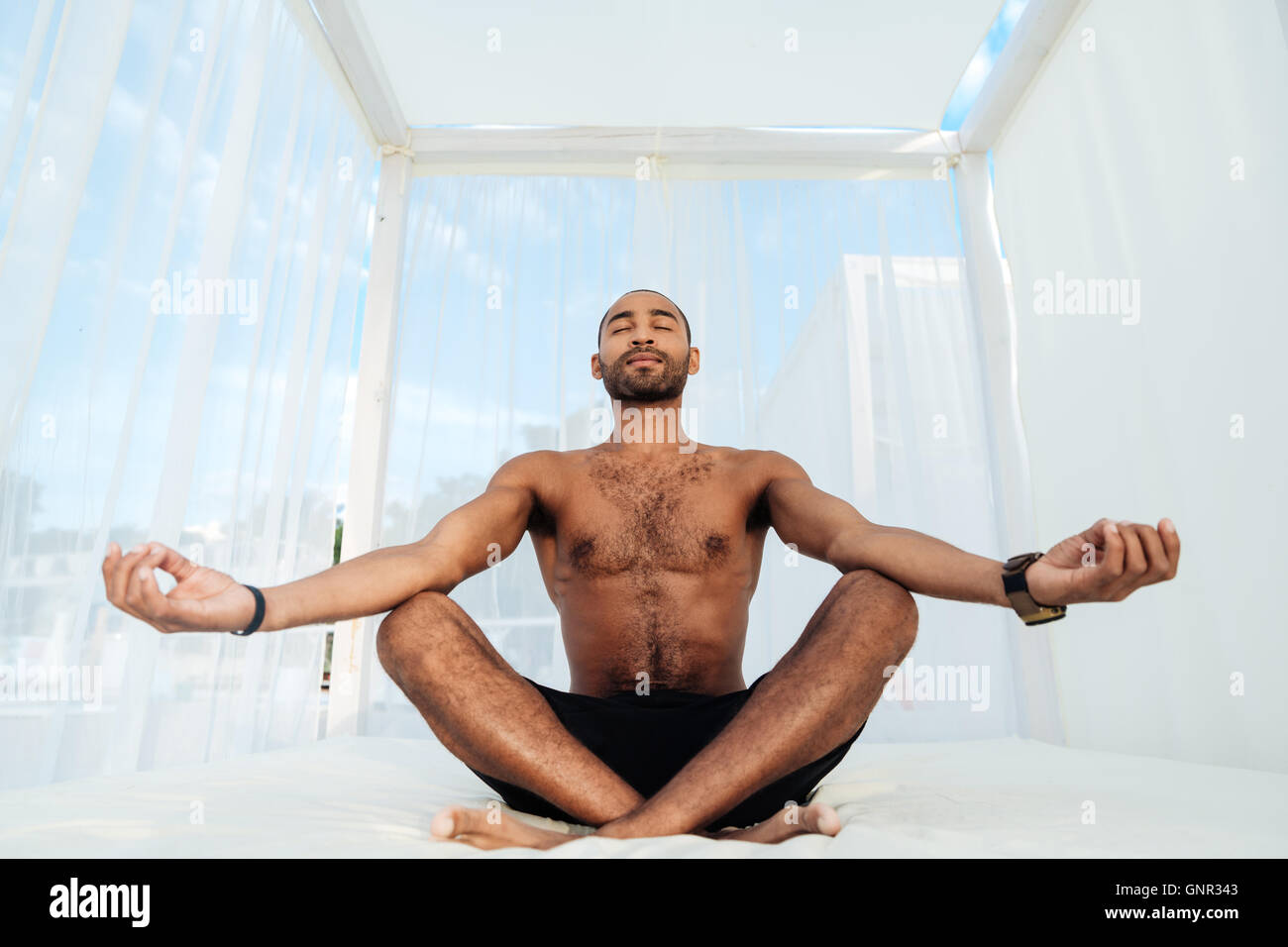 Handsome young african man in shorts sitting and meditating on the ...