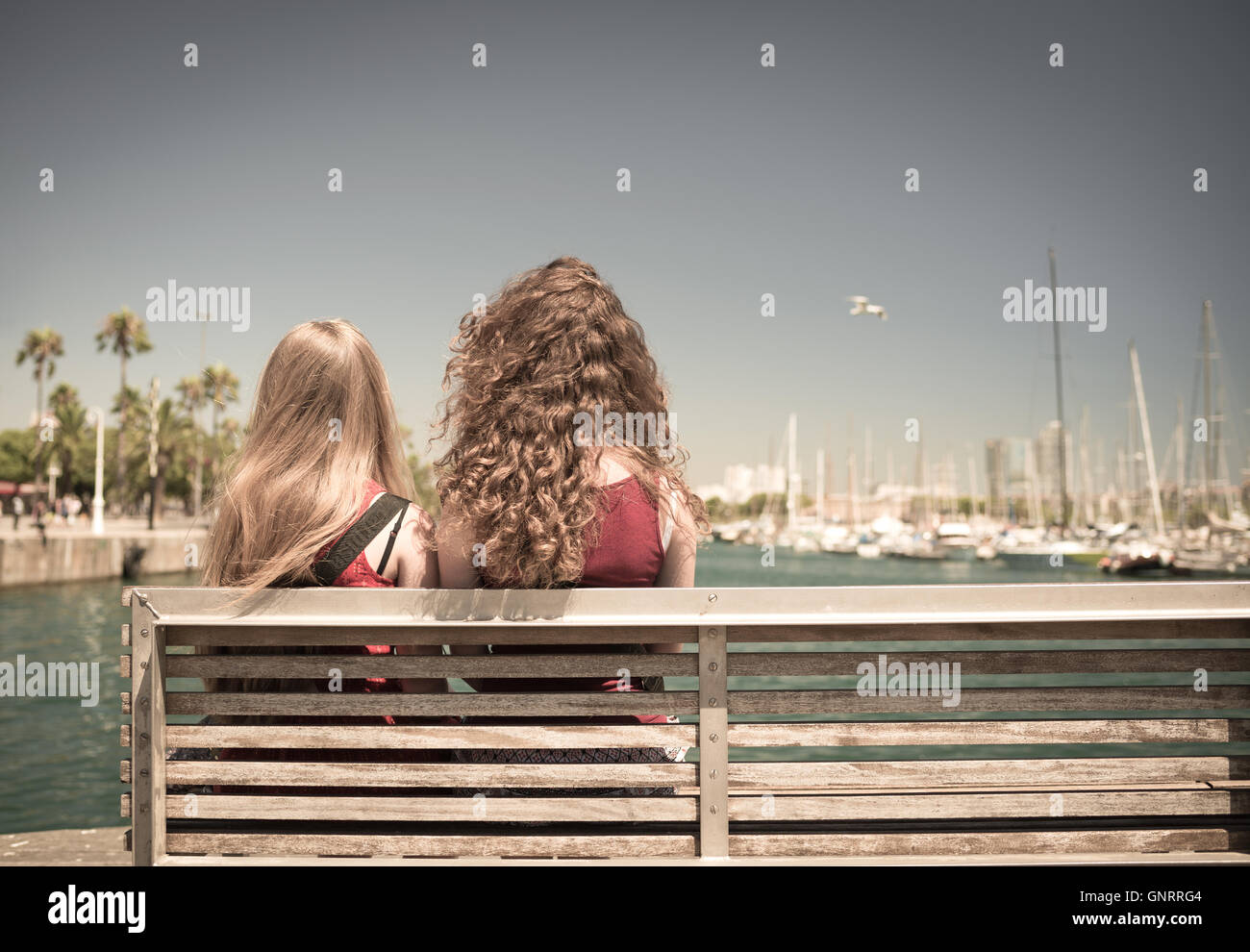 Two girls sitting on the bench watching the port of Barcelona - Spain ...