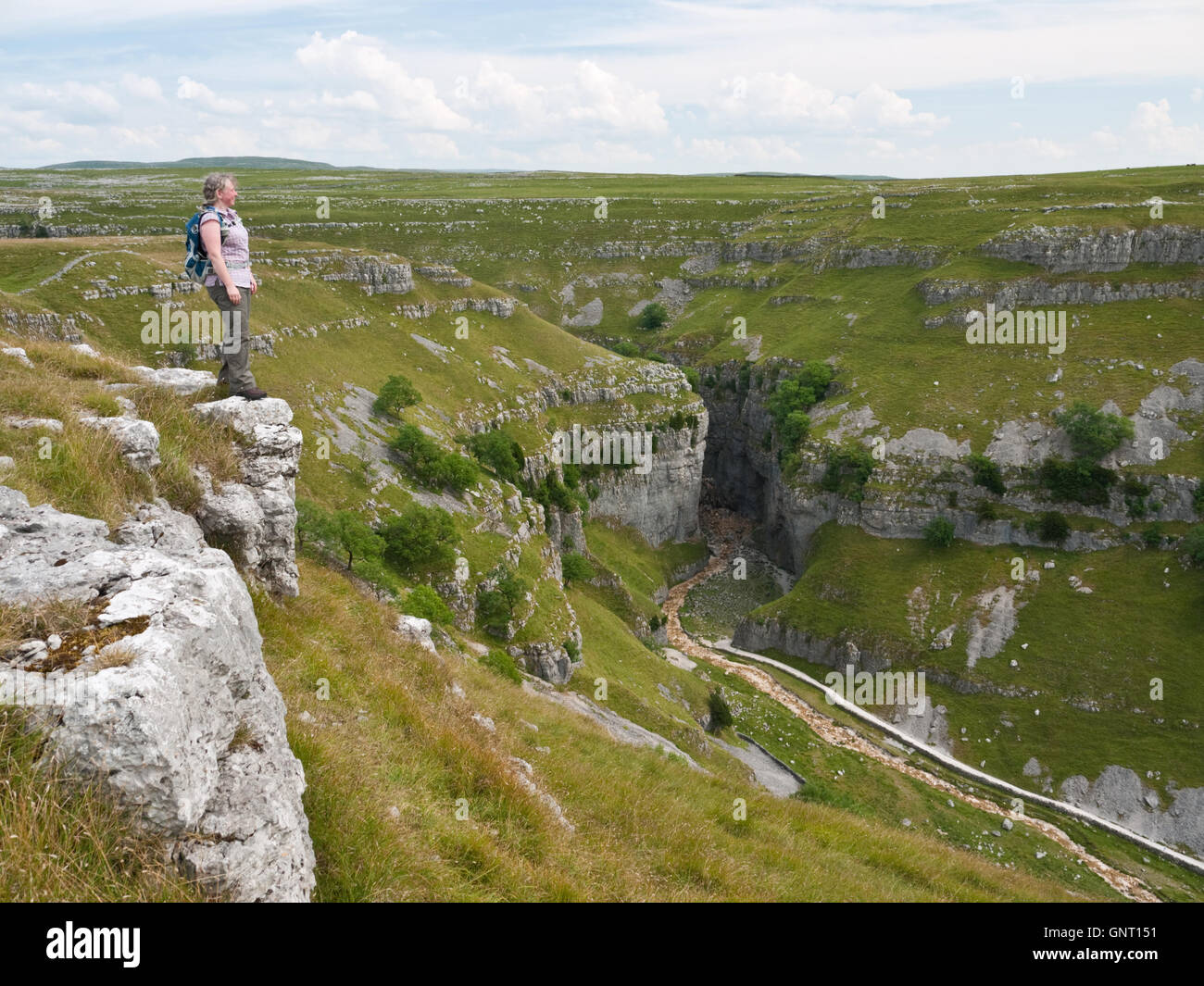 A female hiker admires the view into Gordale Scar, a limestone gorge ...