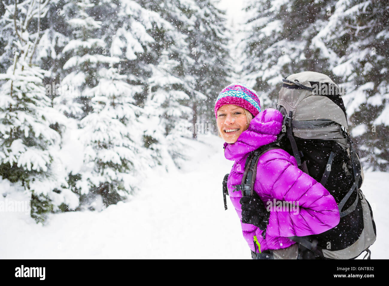 Happy young woman hiking in white winter forest woods with backpack ...