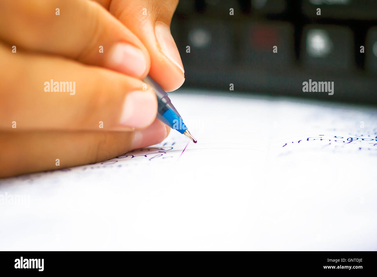 Human hand holding pen on white paper with keyboard in the back ground ...