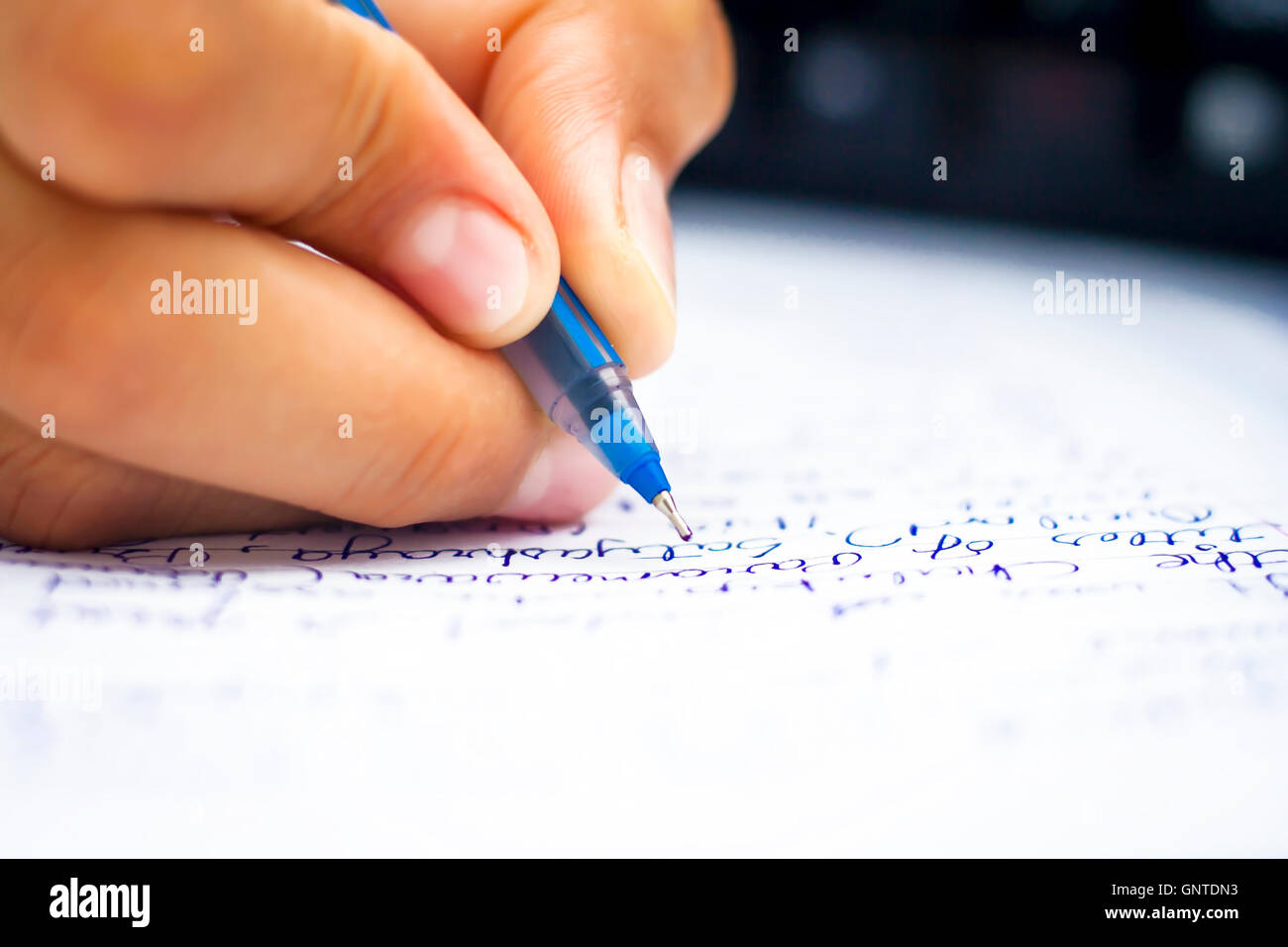 Human hand holding pen on white paper with keyboard in the back ground ...