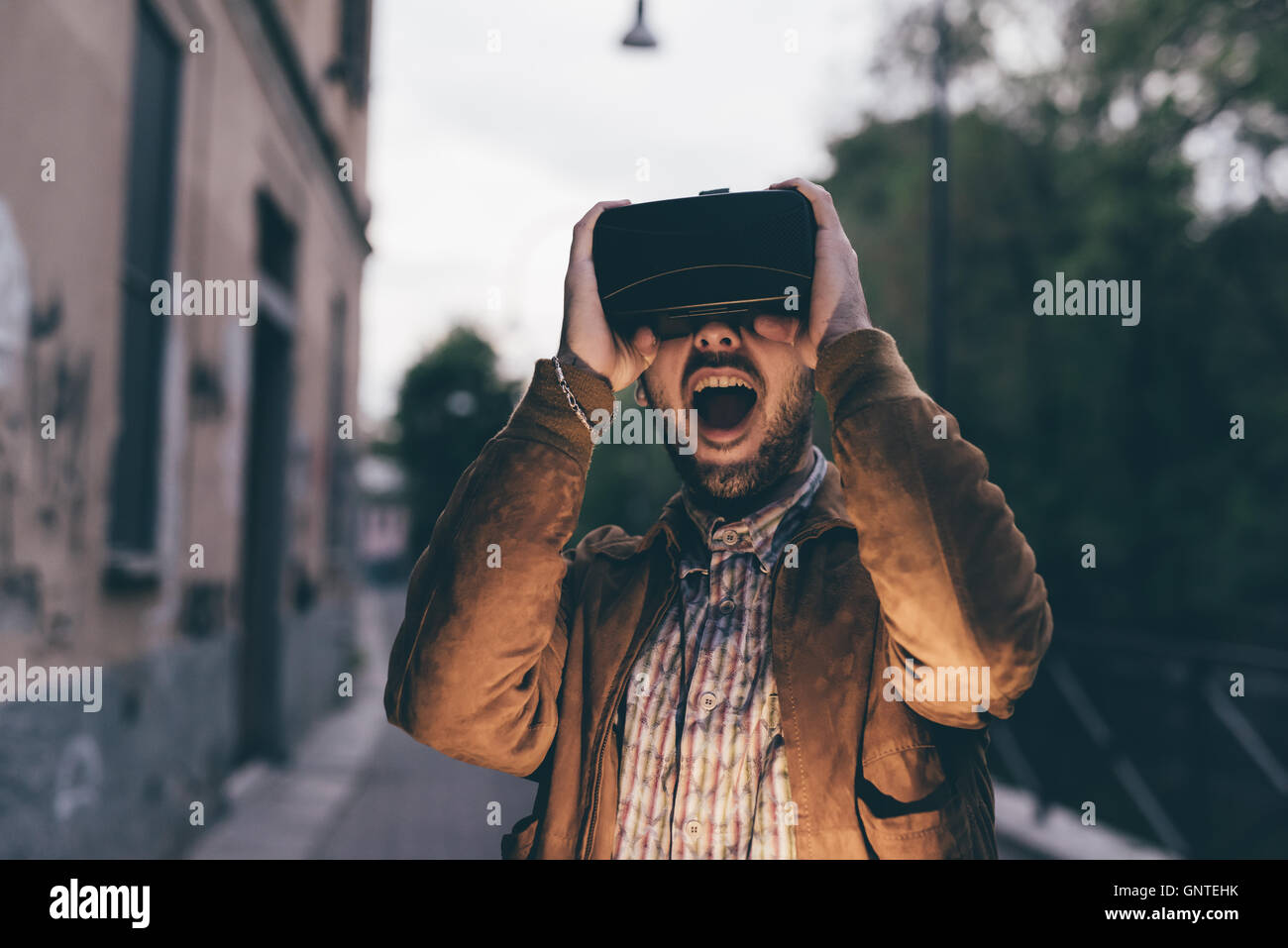 Young man caucasin using 3D viewer looking up surprised in city night ...