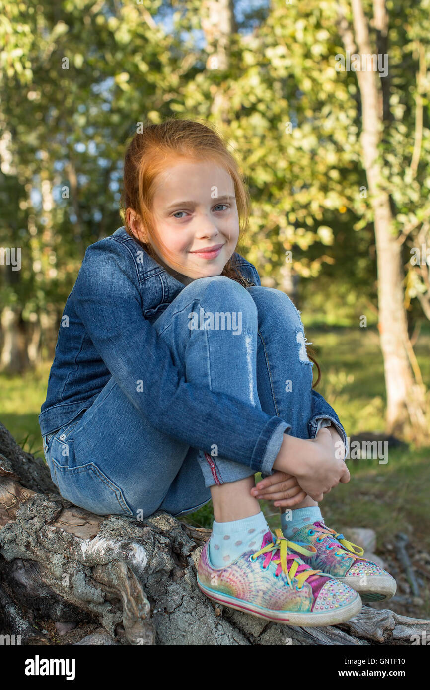 Portrait of a little girl sitting on the roots of a tree Stock Photo ...
