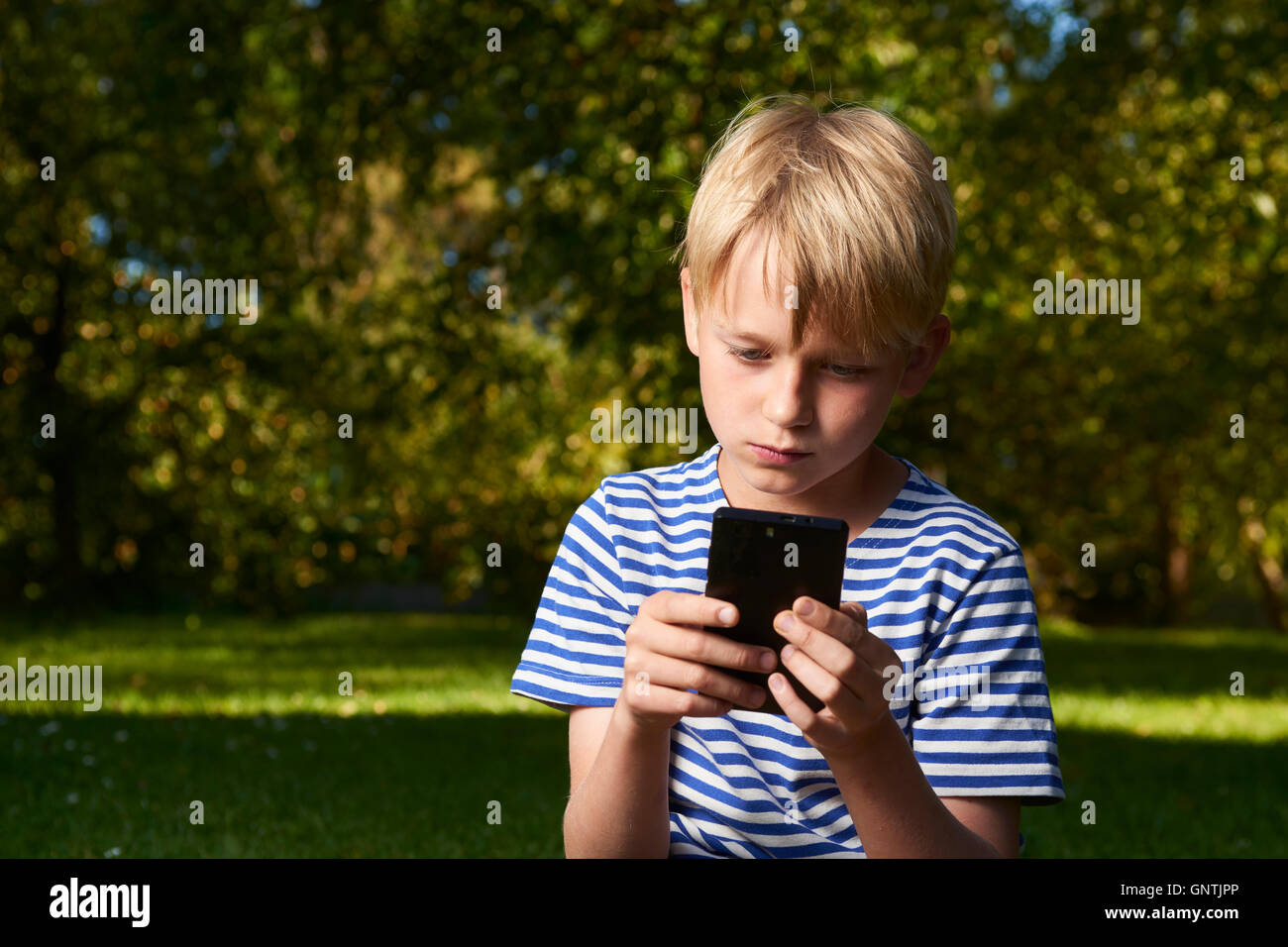 Child young boy with mobile phone outdoor. Child looking at the screen ...
