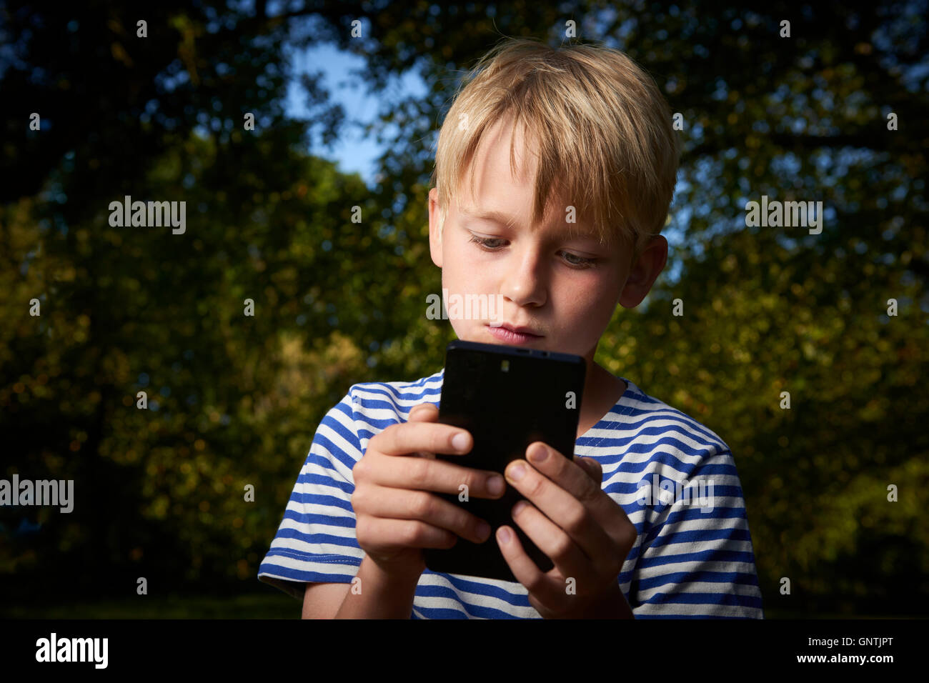 Child young boy with mobile phone outdoor. Child looking at the screen ...