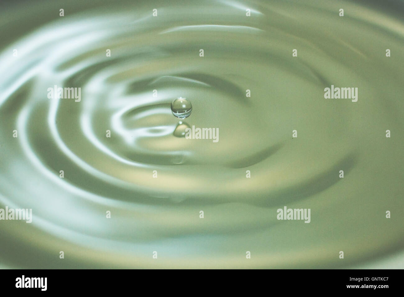 Sphere of Water drop falling towards a cup of still, smooth liquid ...