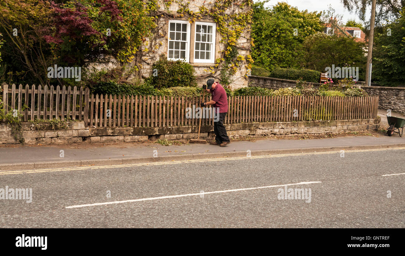 A man cleaning the pathway with a sweeping brush outside a house in ...